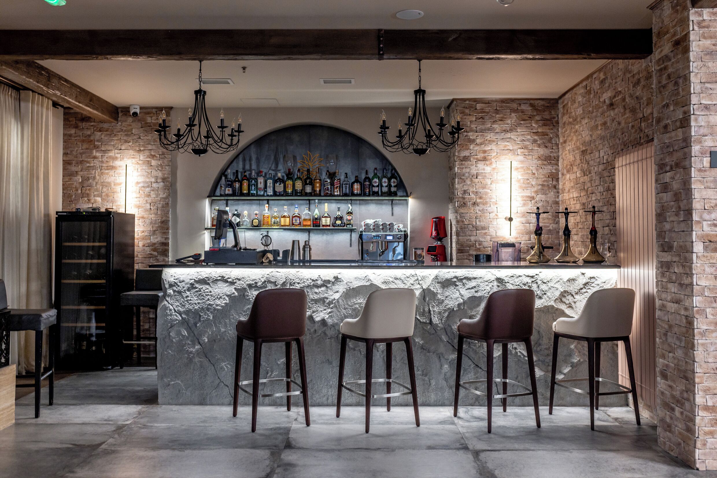 Uma área de bar com balcão de pedra, banquetas e diversas garrafas.