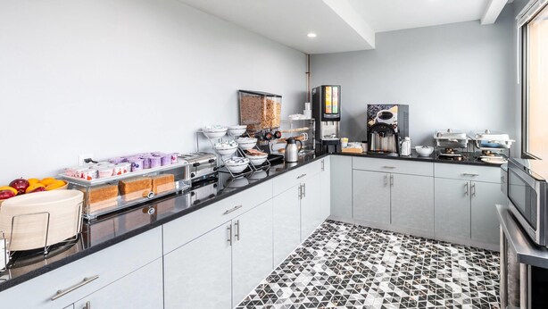 Cozinha moderna com piso quadriculado preto e branco, uma cafeteira e diversos alimentos sobre o balcão.