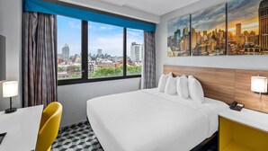 Quarto de hotel com uma cama grande, uma escrivaninha, uma cadeira e vista para a cidade.