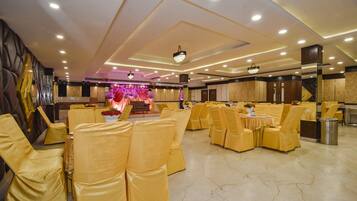 Uma sala de banquetes com mesas redondas, cadeiras amarelas e um palco com decorações florais.