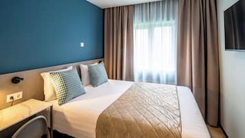 Quarto de hotel com cama, escrivaninha e televisão.