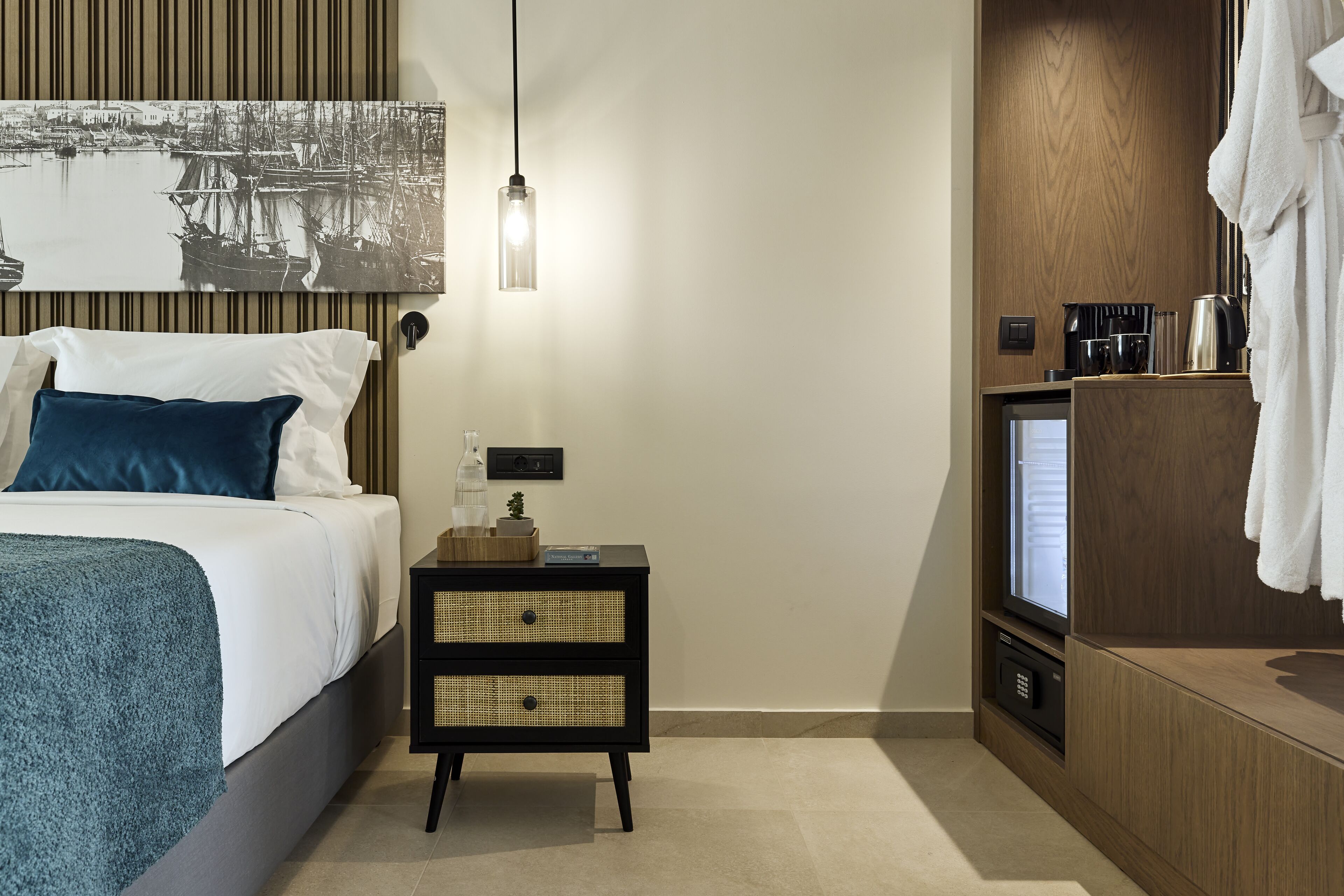 Quarto de hotel com cama, mesa de cabeceira, televisão e um quadro pendurado na parede.