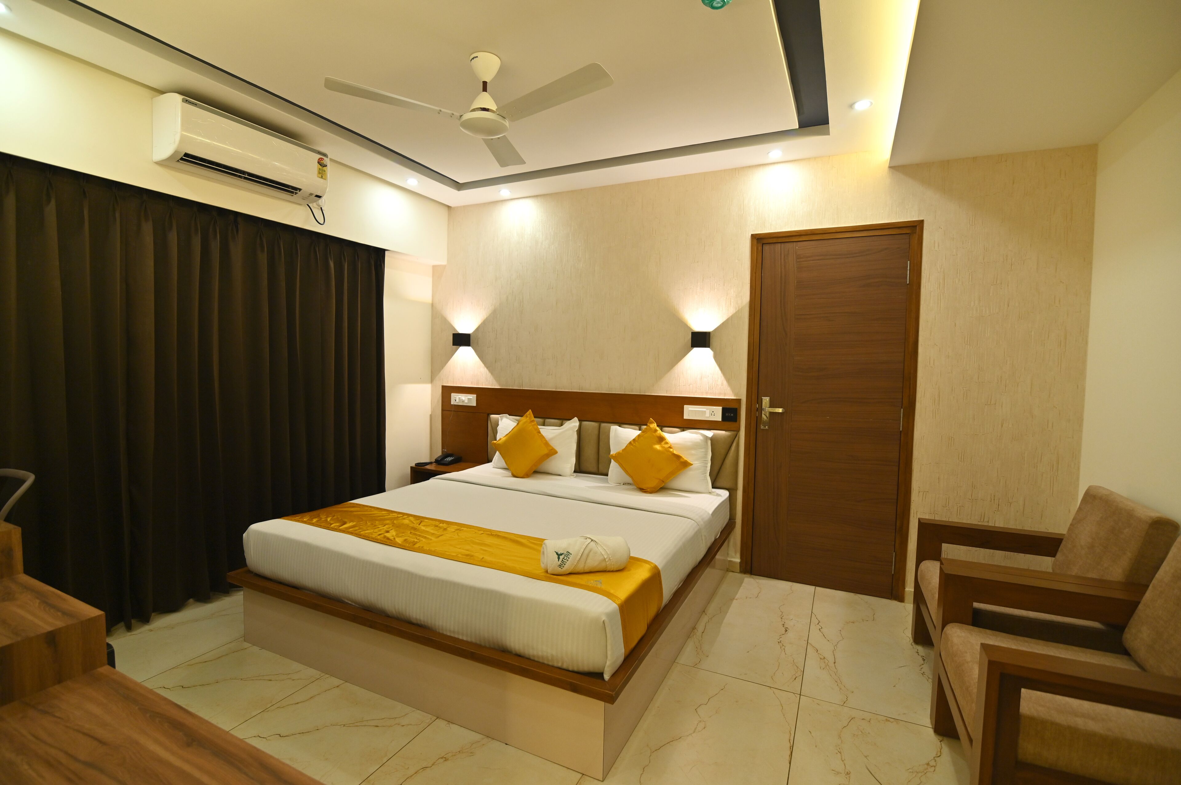 Quarto de hotel com cama, escrivaninha, cadeira, guarda-roupa e ventoinha no teto.