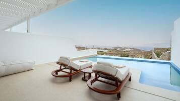 Espaço lounge ao ar livre moderno, com duas poltronas e uma mesinha, com vista para uma piscina e paisagem deslumbrante.