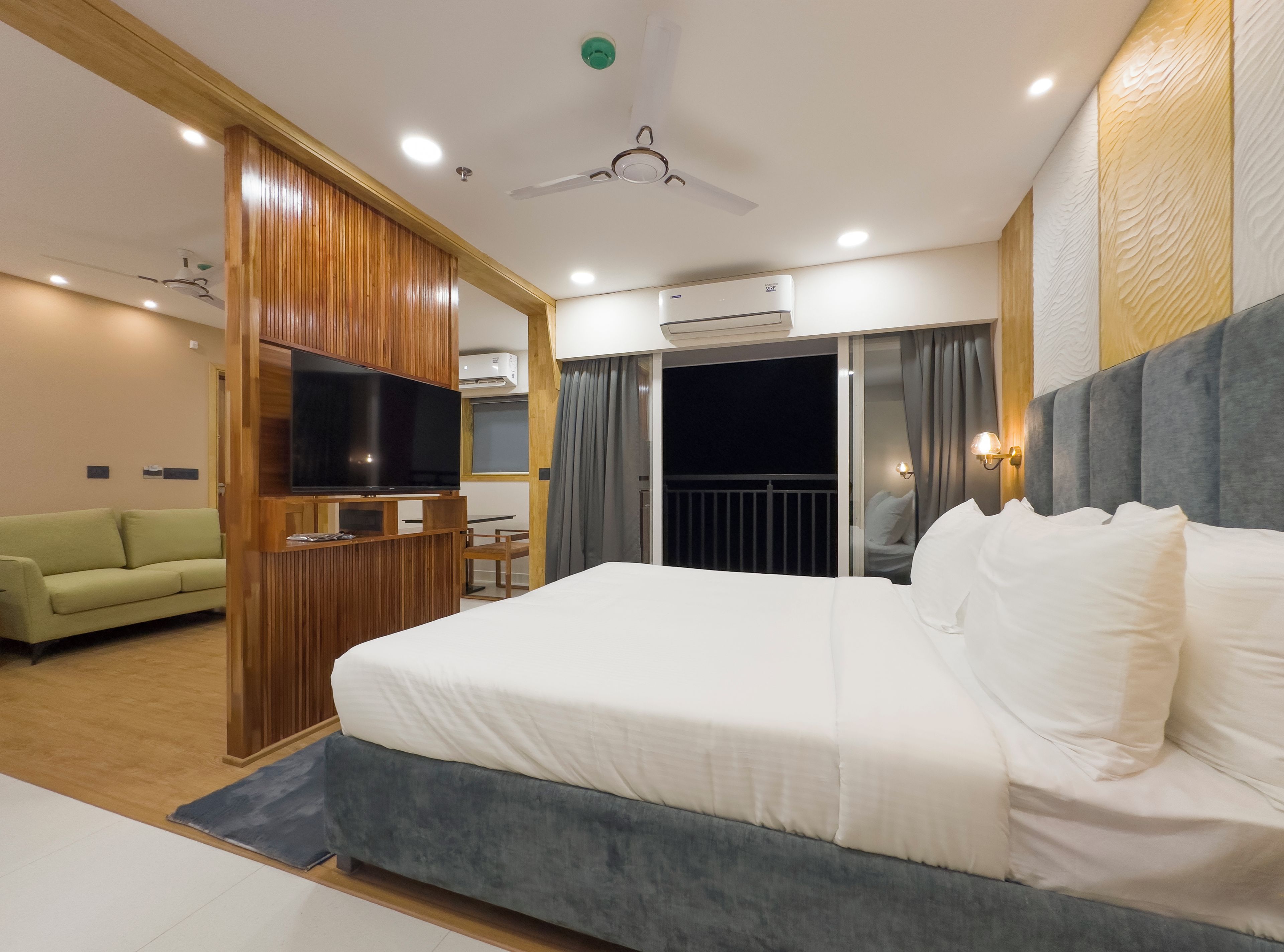 Quarto de hotel moderno com cama grande, televisão, ventoinha de teto e ar condicionado.