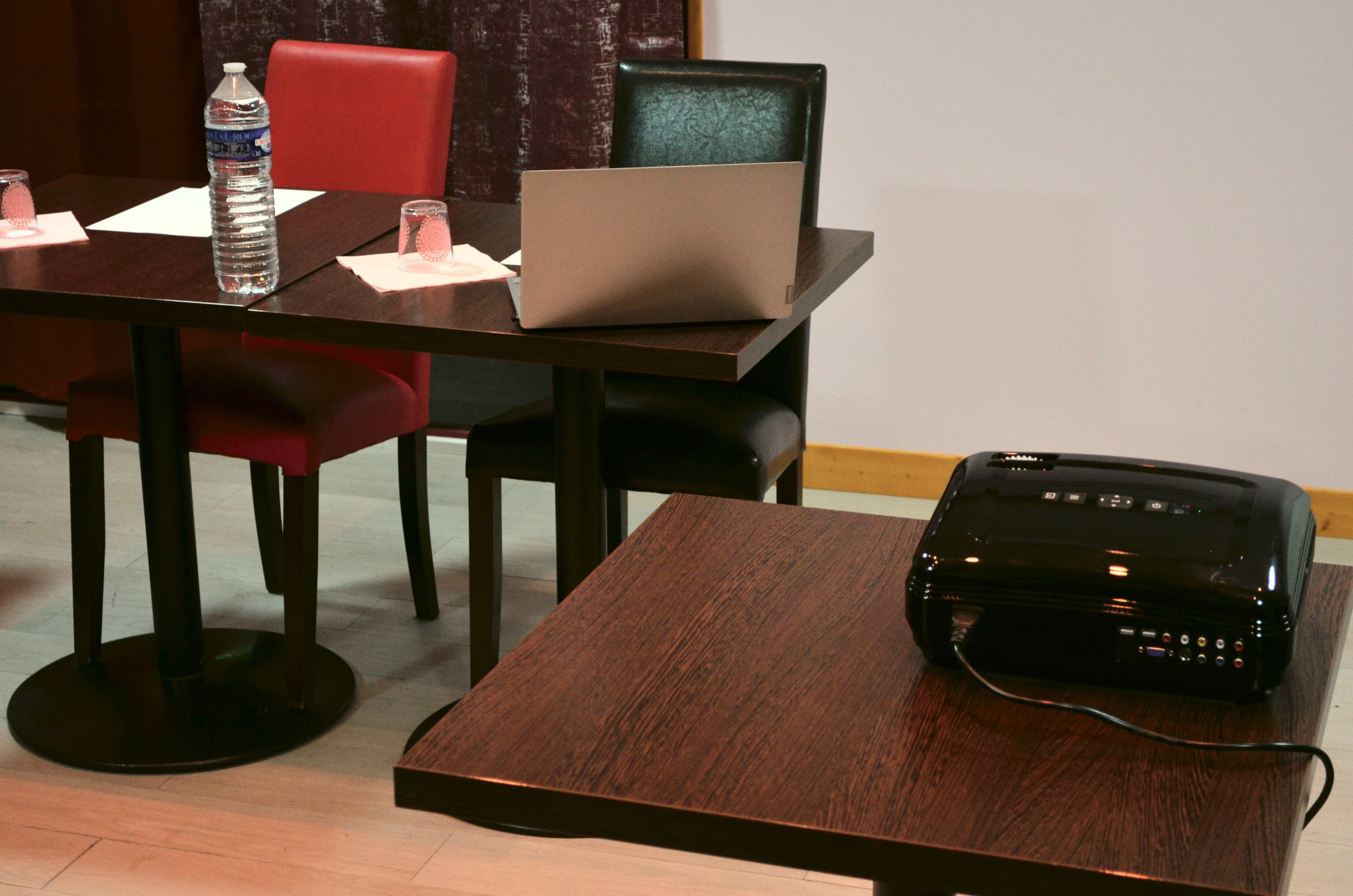Uma sala de conferências com um laptop, um projetor e uma garrafa de água sobre a mesa.