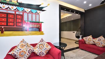 Uma sala de estar moderna com sofás vermelhos, almofadas estampadas, uma mesa redonda pequena e uma parede decorativa com design tradicional.