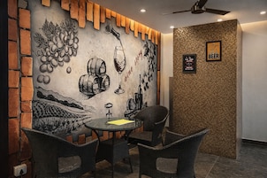 Interior de restaurante com um mural de vinho e uvas, cadeiras de vime e uma mesa com um guardanapo amarelo.