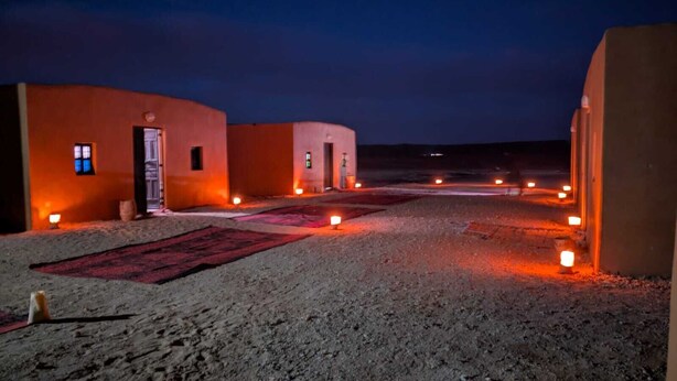 Um complexo de edifícios em estilo desértico à noite, com caminhos e portas iluminados.