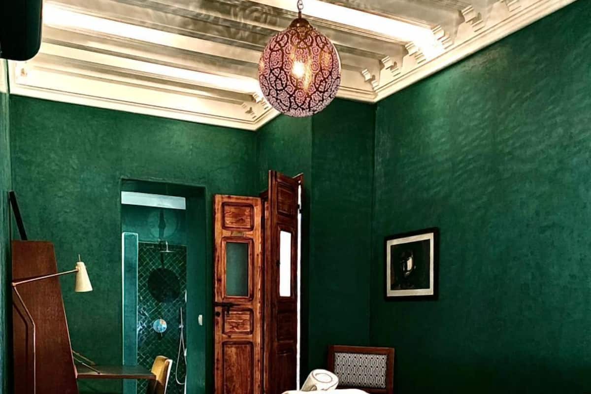 Quarto com cama, escrivaninha, cadeira, luminária pendente e porta.
