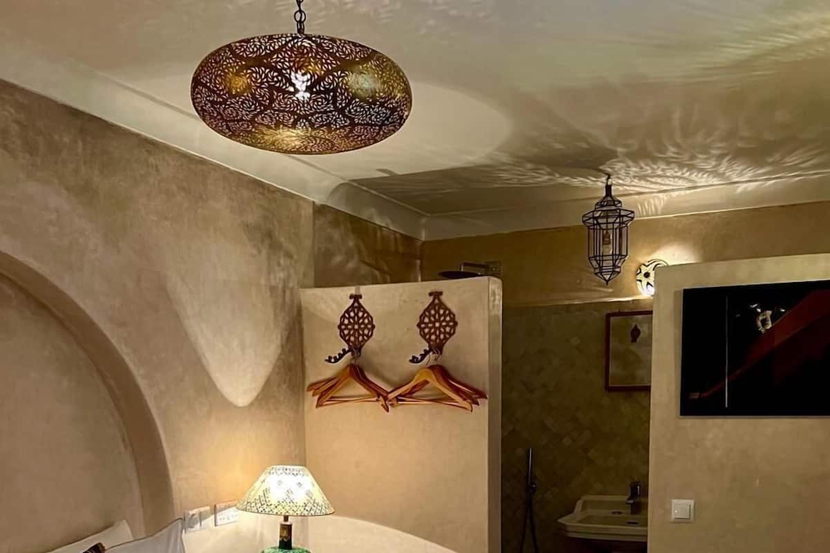 Quarto de hotel com cama, luminária, luminária pendente e suporte de toalha fixado na parede.
