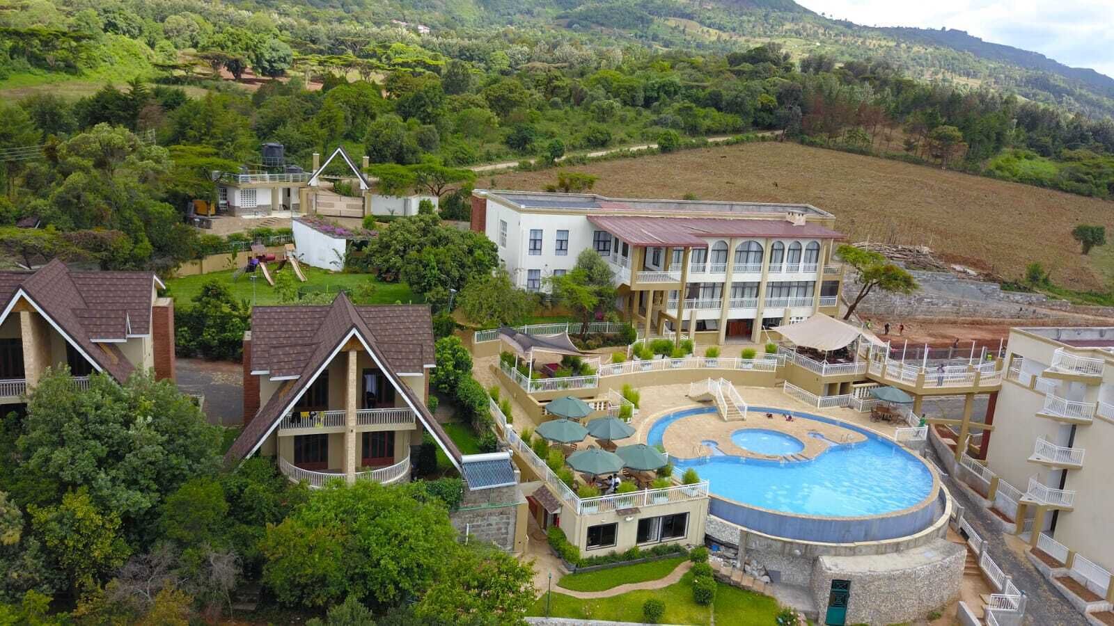 Um resort com vários edifícios, uma piscina central e vegetação ao redor.