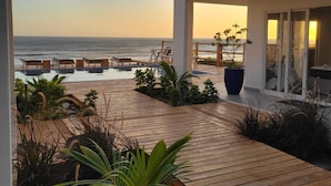 Um deck de madeira com cadeiras de lounge e vista para o oceano ao pôr do sol.
