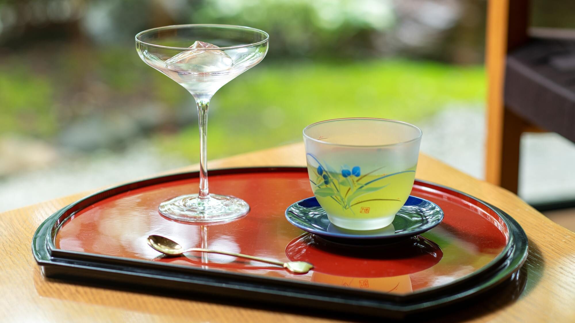 Uma bandeja com uma taça de martini e uma chávena com motivos florais, colocada sobre uma mesa de madeira.