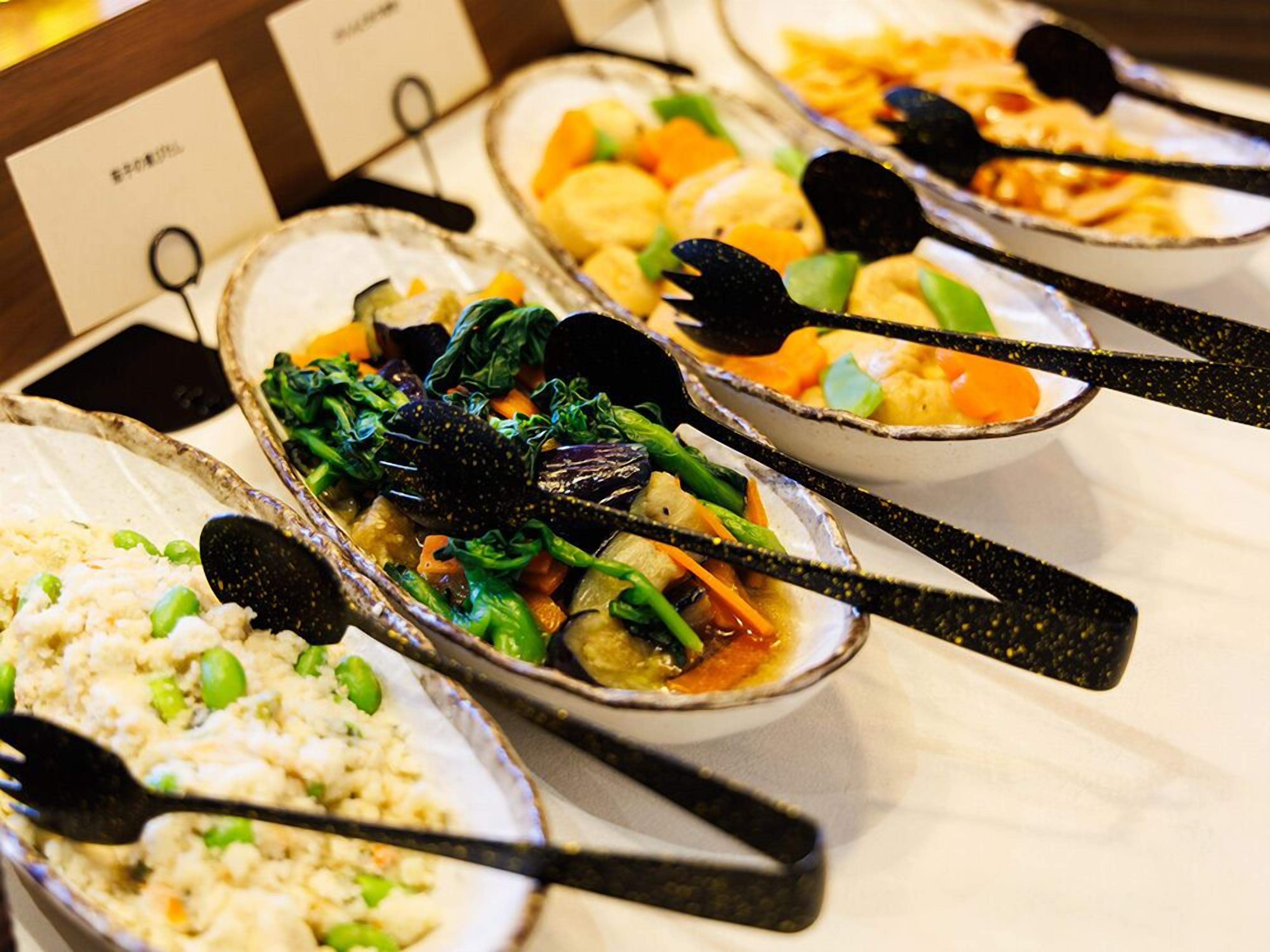 Buffet com diversos pratos servidos em conchas de ostras, incluindo frutos do mar, legumes e arroz.