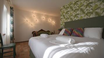 Uma cama bem arrumada com roupa de cama branca, cabeceira verde e papel de parede estampado ao fundo.