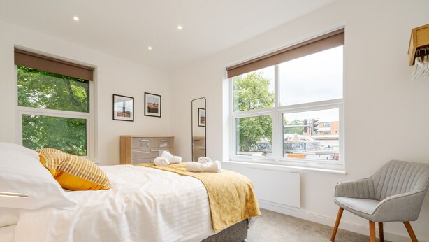 Quarto moderno com cama, uma cadeira e janelas amplas com vista para o exterior.