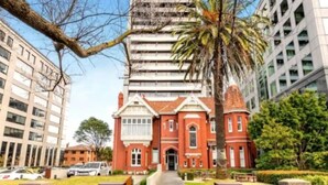 Um edifício de tijolos vermelhos com uma entrada central, cercado por edifícios modernos e altos.