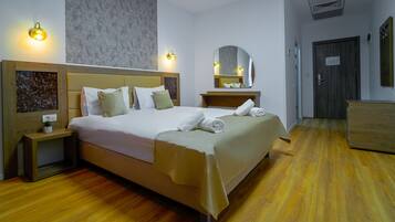 Quarto de hotel com uma cama grande, mesas de cabeceira, cômoda de madeira, espelho e arandelas.