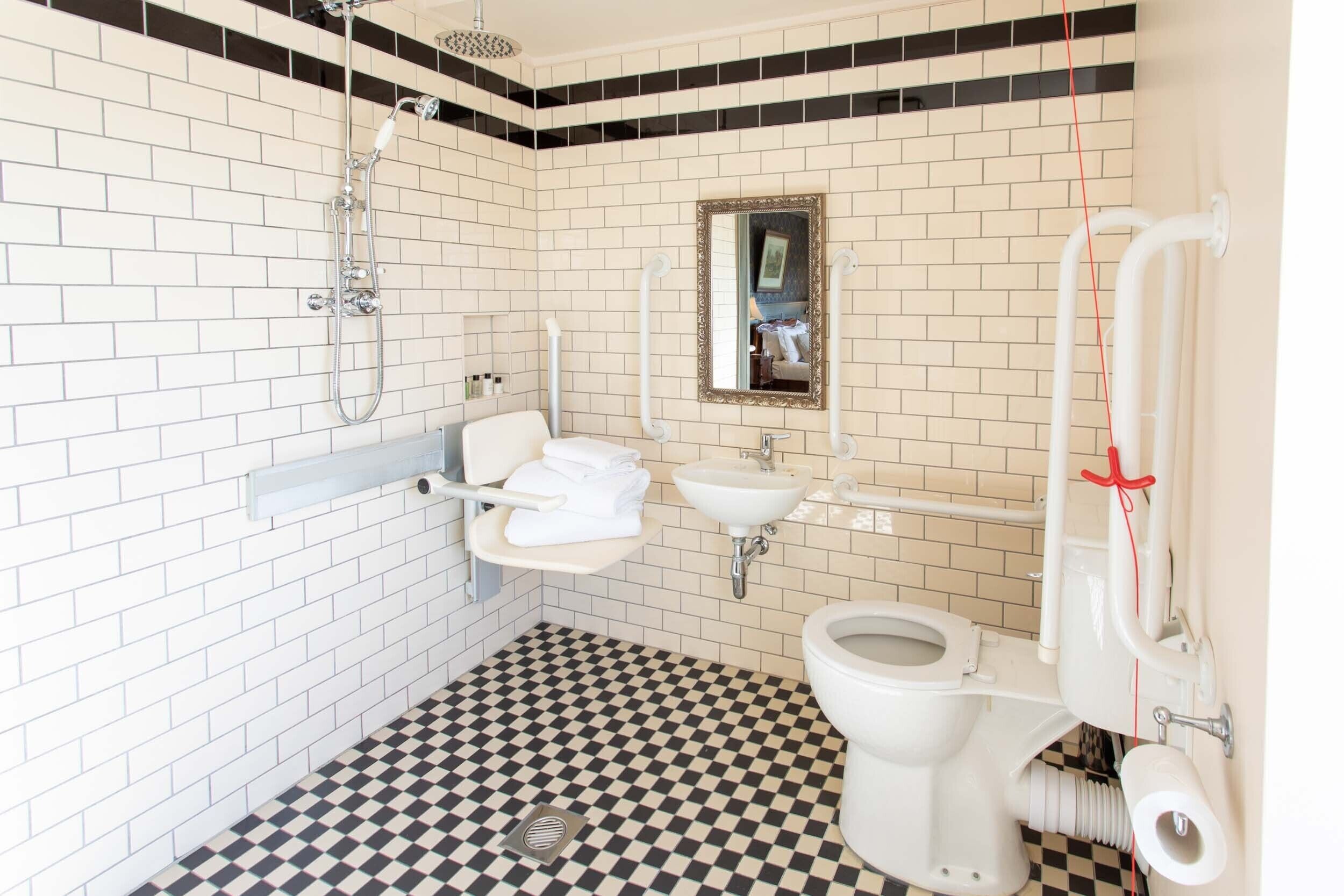 Casa de banho com paredes em azulejos brancos, chão em padrão xadrez preto e branco, sanita branca, lavatório e cabine de duche.