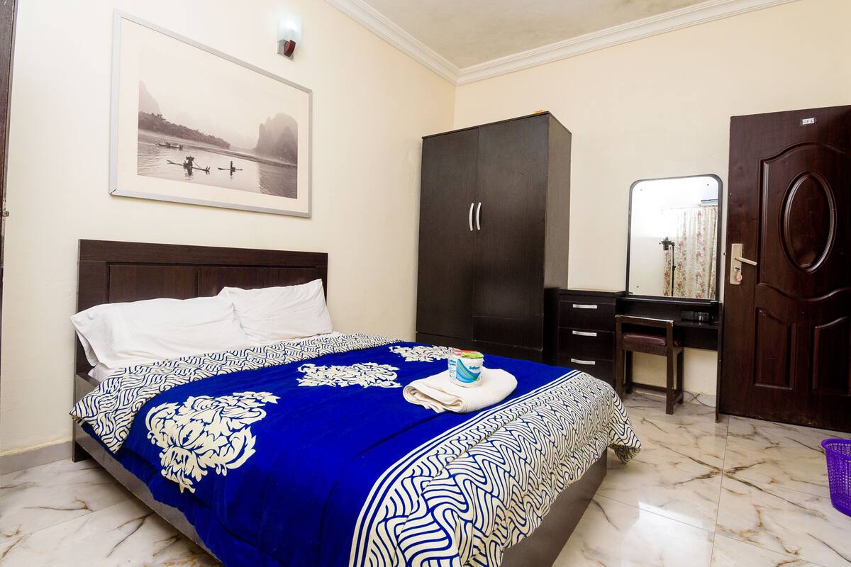 Quarto de hotel com cama, guarda-roupa, escrivaninha e espelho de banheiro.