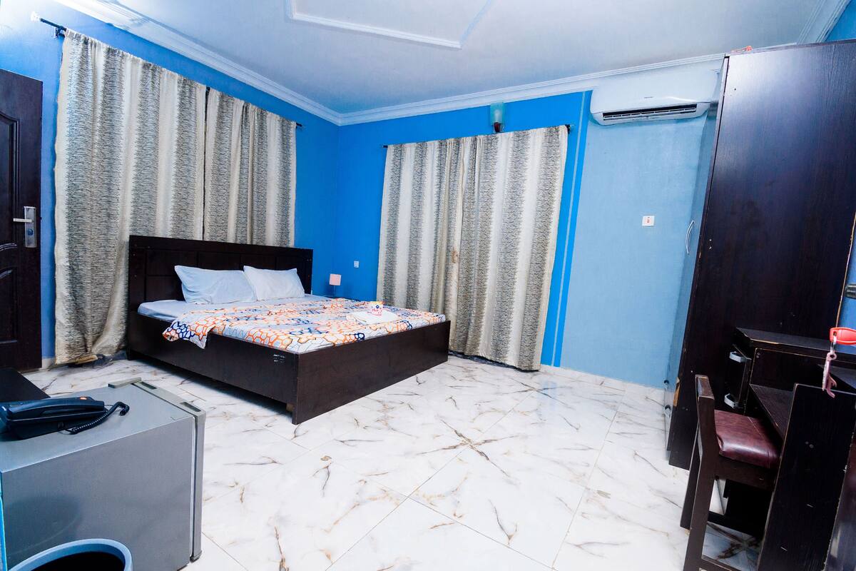 Um quarto com cama, cortinas, escrivaninha e guarda-roupa.
