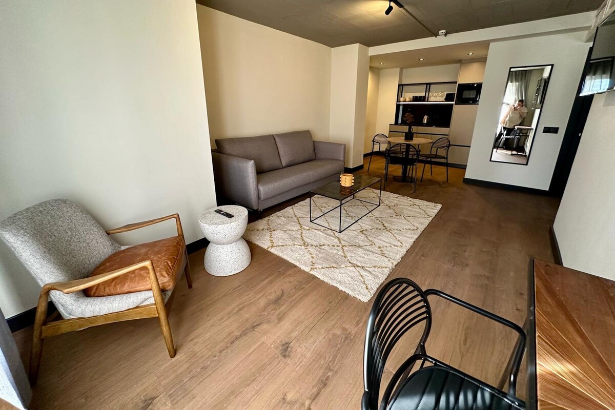 Uma sala de estar moderna com um sofá cinzento, poltrona de madeira e uma mesa de centro pequena.