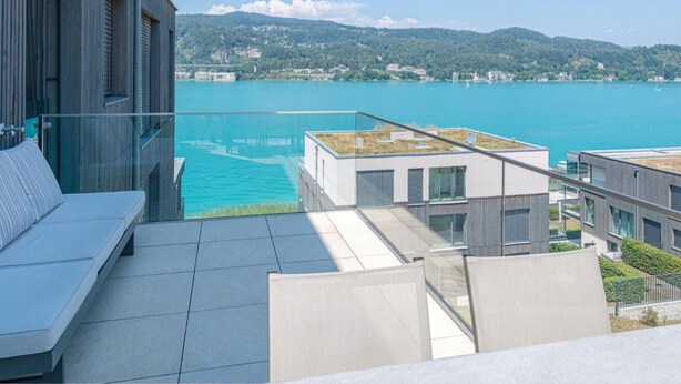 Varanda moderna com vista para um lago e montanhas ao longe.