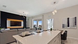 Uma cozinha moderna com uma ilha grande, uma área de jantar com balcão e uma sala de estar com sofá e televisão.
