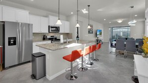 Cozinha moderna com eletrodomésticos de aço inoxidável, bancada de granito e uma ilha central com banquetas.