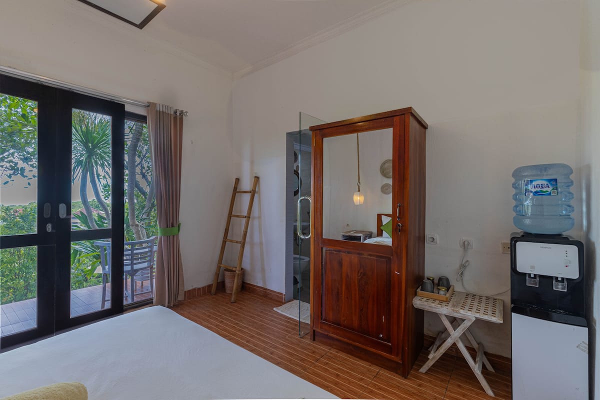 Quarto com cama, armário de madeira, dispensador de água e vista para o verde lá fora.