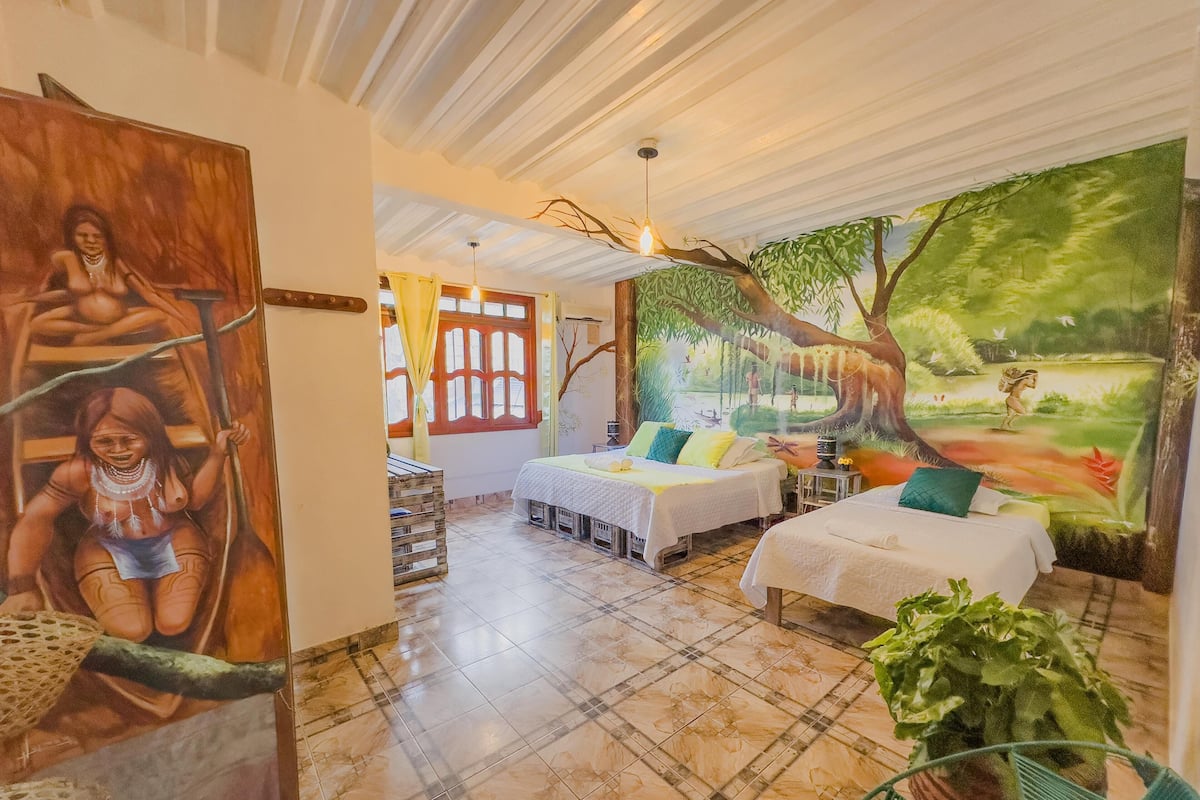 Quarto com duas camas, um mural grande e vista para uma floresta.