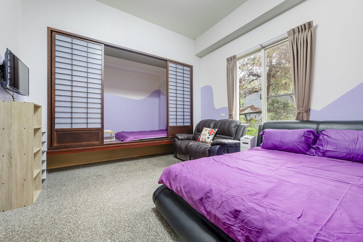 Quarto com cama, cadeira, televisão e porta deslizante.