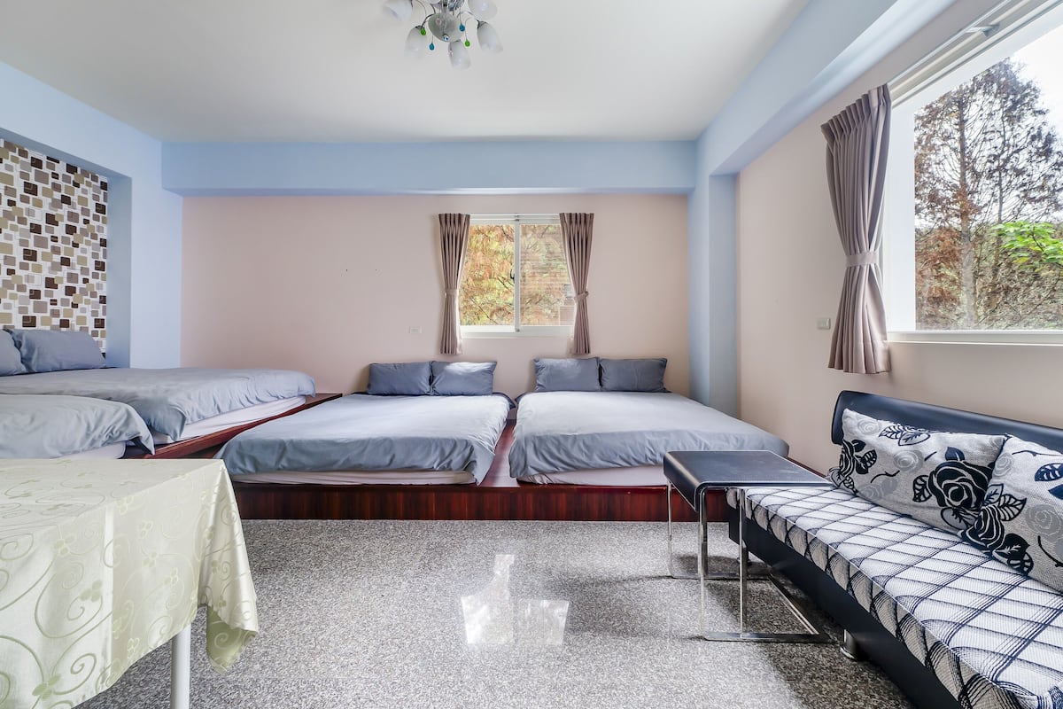 Quarto com duas camas, um sofá, uma mesa e uma janela com cortinas.