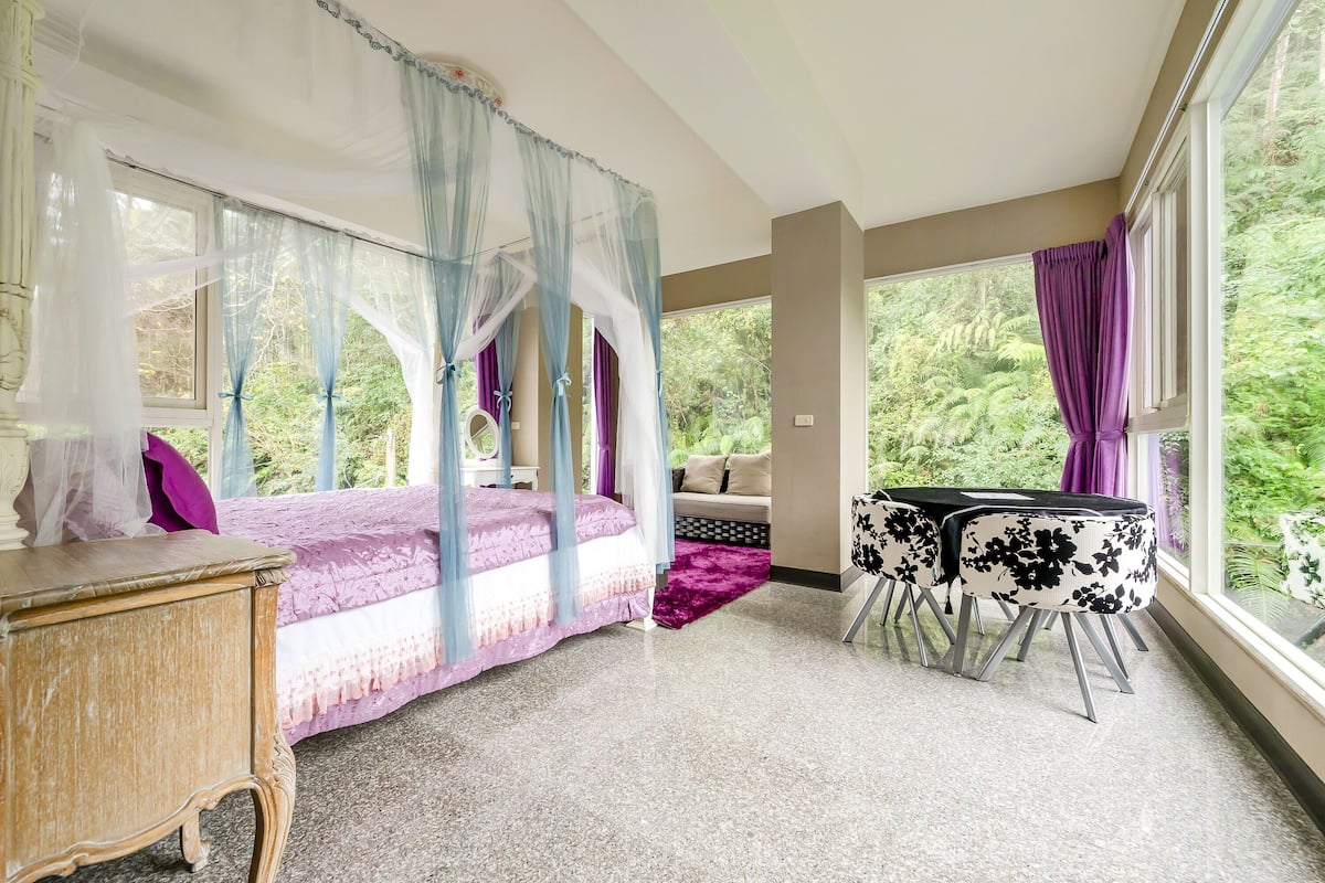 Quarto com cama, escrivaninha e vista para o verde.