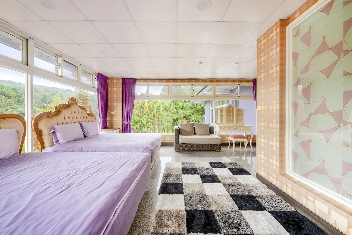 Quarto com duas camas, um sofá e uma janela grande com vista para o verde.