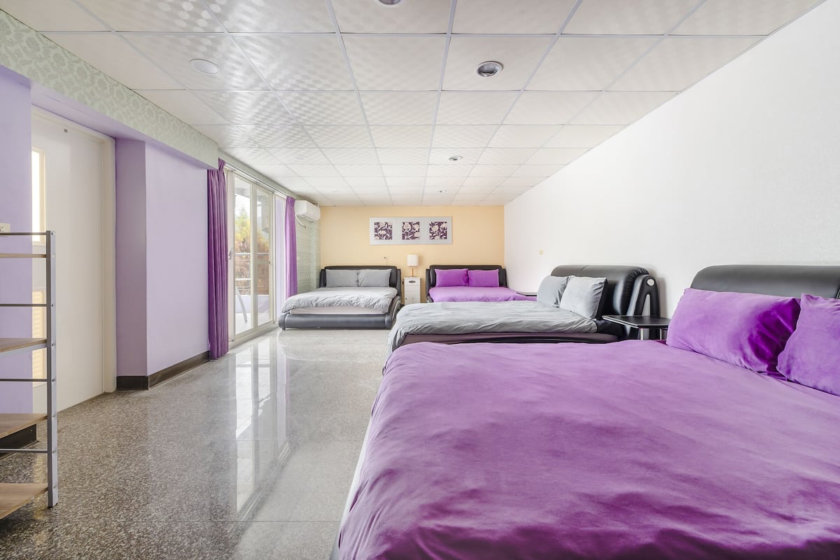 Quarto de hotel com duas camas, uma escrivaninha, uma cadeira e uma janela com cortinas.