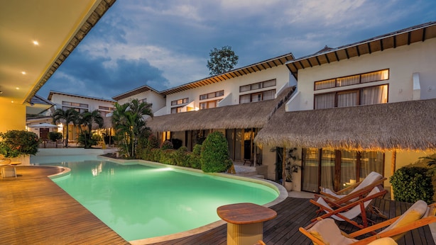 Um resort com piscina, deck de madeira e edifícios com telhado de palha.