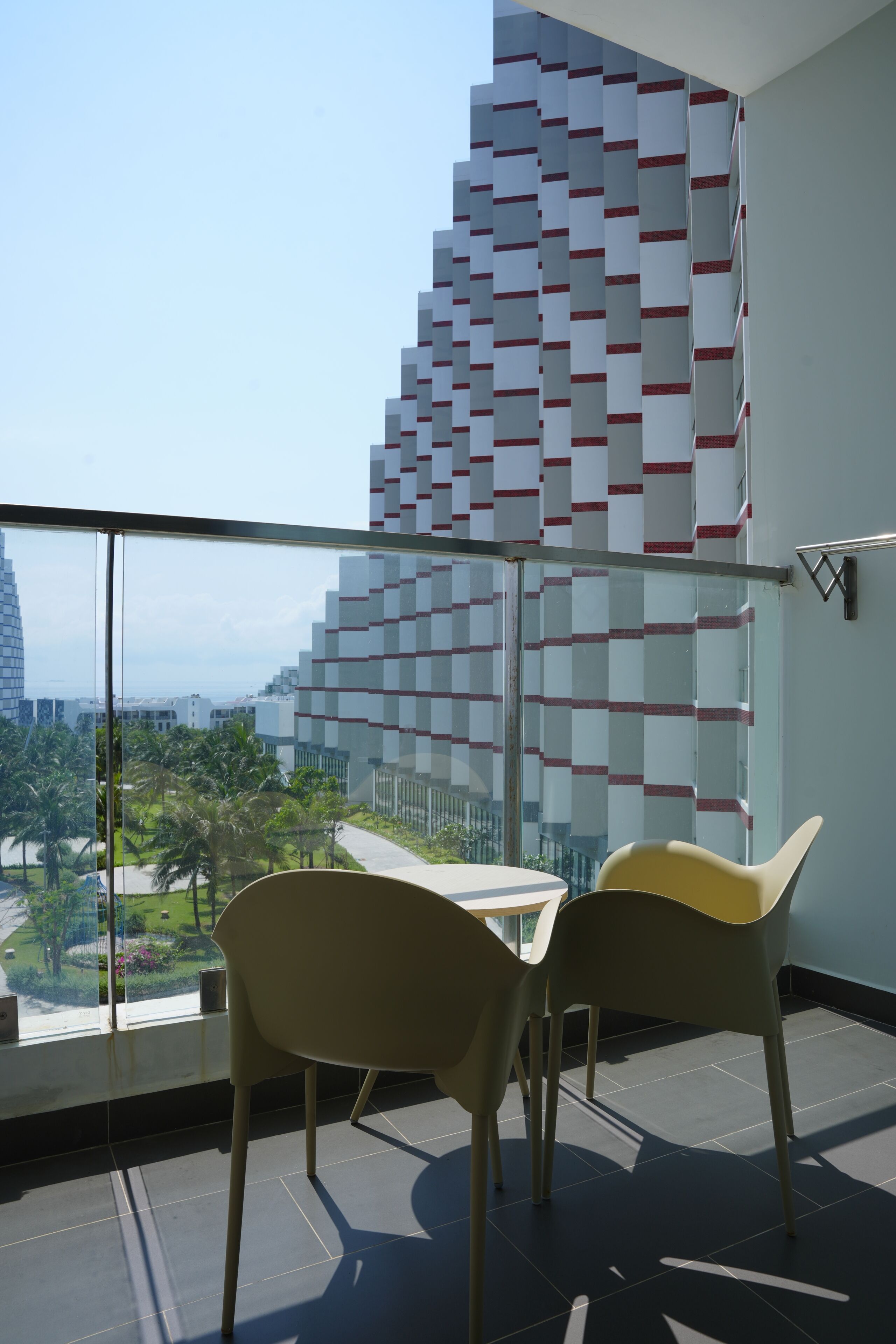 Varanda com duas cadeiras, uma mesa e vista para um edifício moderno com fachada geométrica.