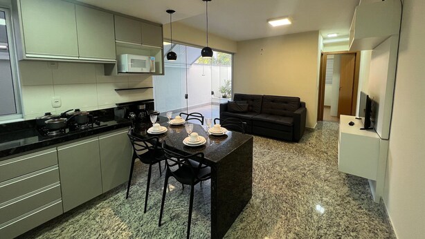 Cozinha moderna com área de jantar, sofá de couro preto e televisão em suporte.