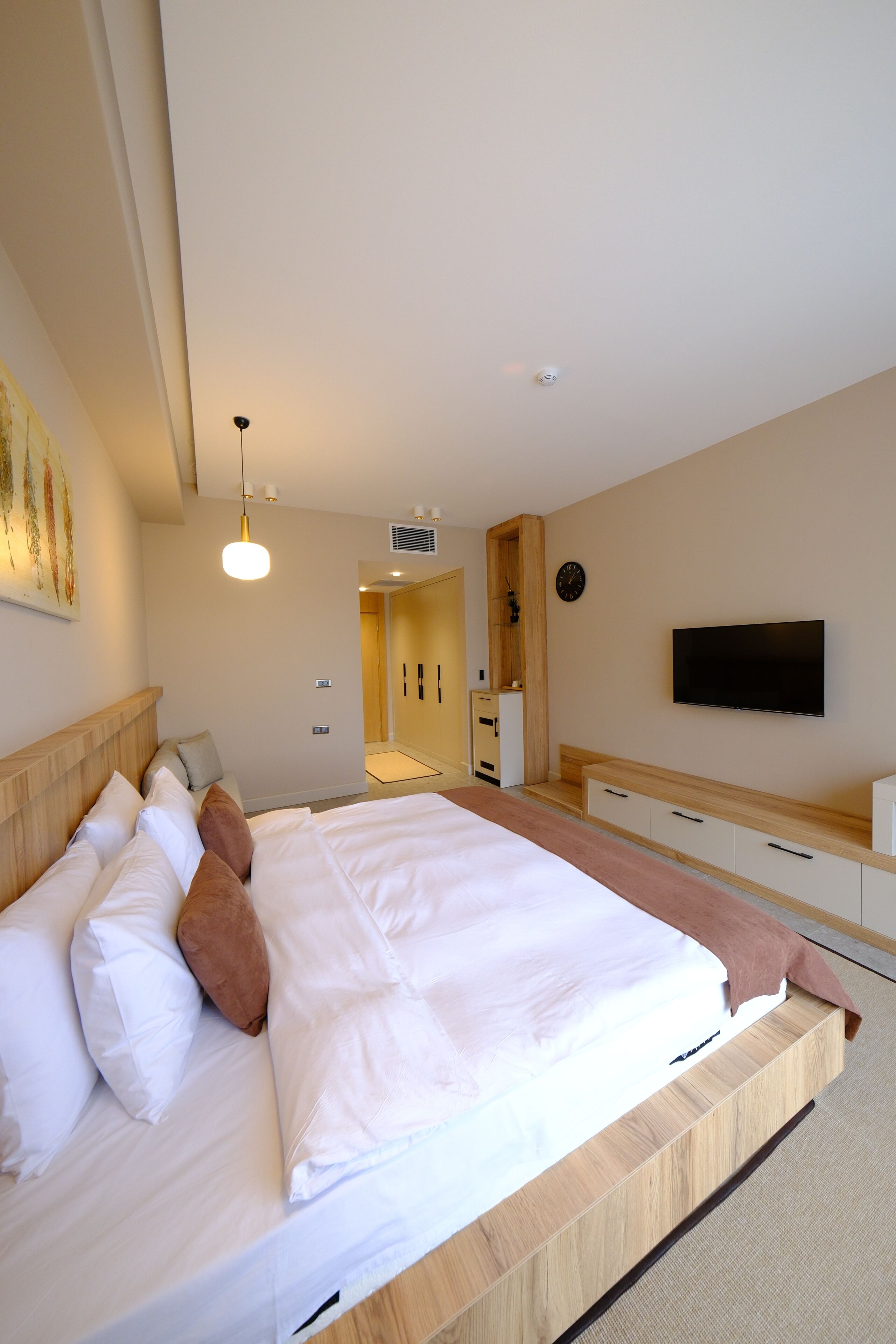 Quarto de hotel moderno com uma cama grande, televisão de tela plana na parede e cabeceira de madeira.