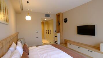 Quarto de hotel moderno com uma cama grande, televisão de tela plana na parede e cabeceira de madeira.