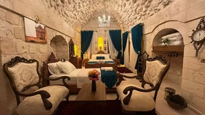 Quarto com uma cama, duas poltronas, uma mesinha com um vaso, um relógio e um espelho na parede.