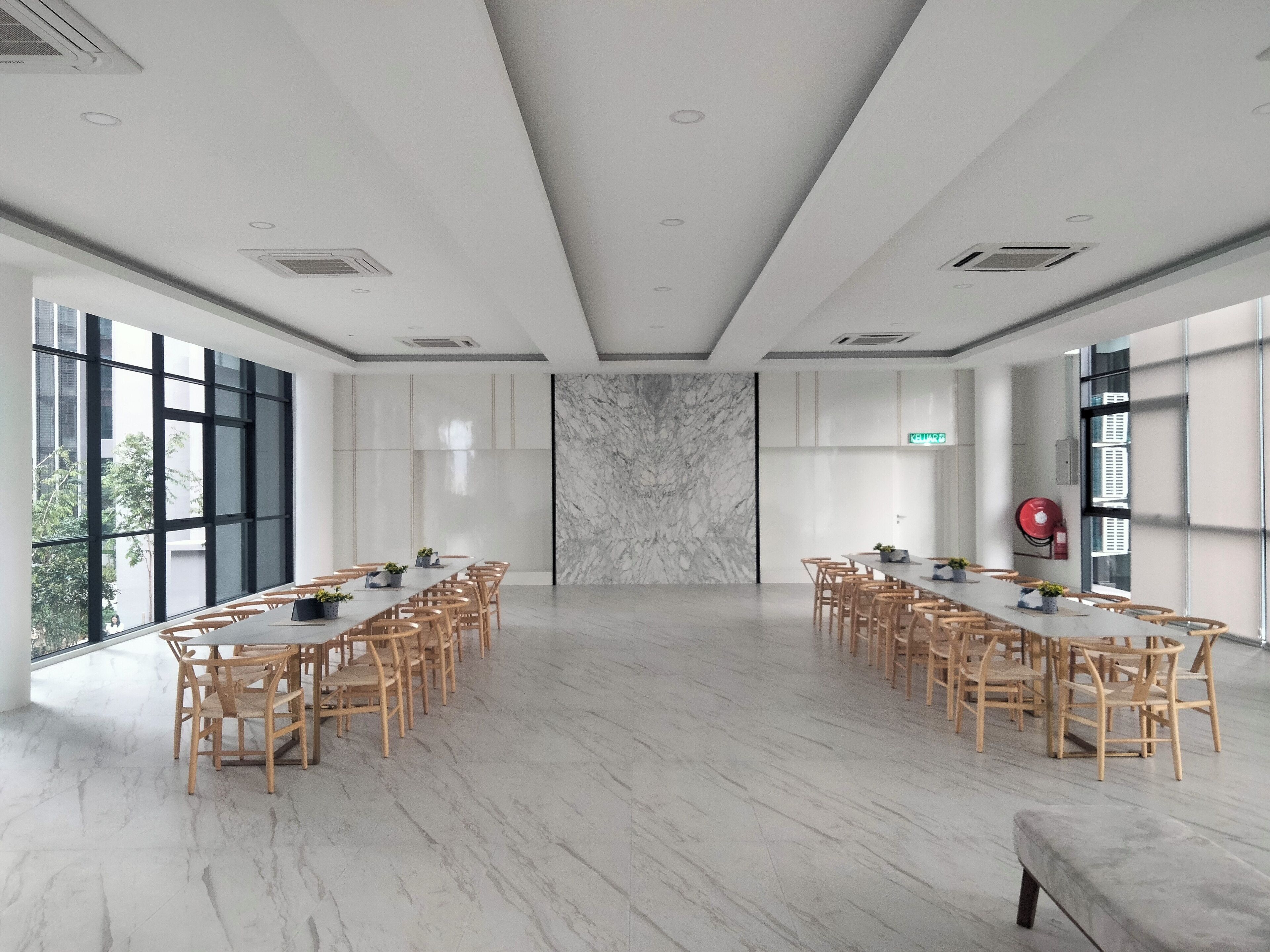 Uma sala de conferências ampla com uma mesa comprida e cadeiras, janelas grandes e uma parede de mármore.