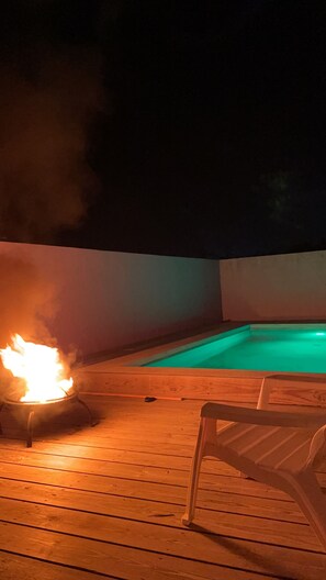 Um deck de madeira com piscina e lareira.