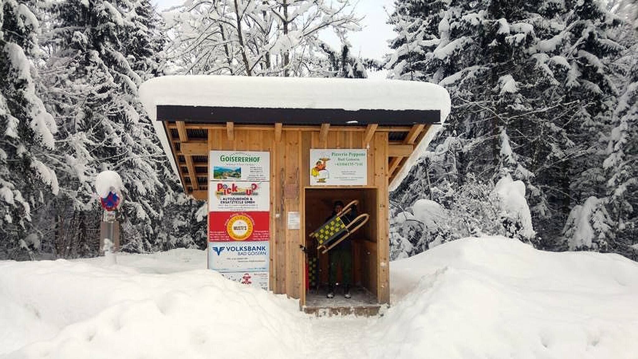 Uma cabana de madeira com telhado coberto de neve, rodeada por árvores cobertas de neve.