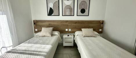 Quarto de hotel com duas camas de solteiro, uma mesinha de cabeceira e um ar condicionado fixado na parede.