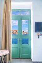 Uma porta verde com vista para uma cidade costeira, uma mesa pequena e uma televisão na parede.