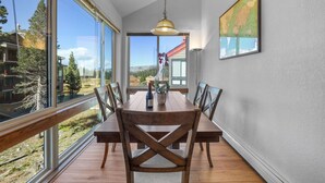 Uma sala de jantar com mesa e cadeiras de madeira, janelas amplas e um lustre.