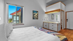 Quarto moderno com uma cama grande, cômoda, espelho e janela com vista para uma casa.